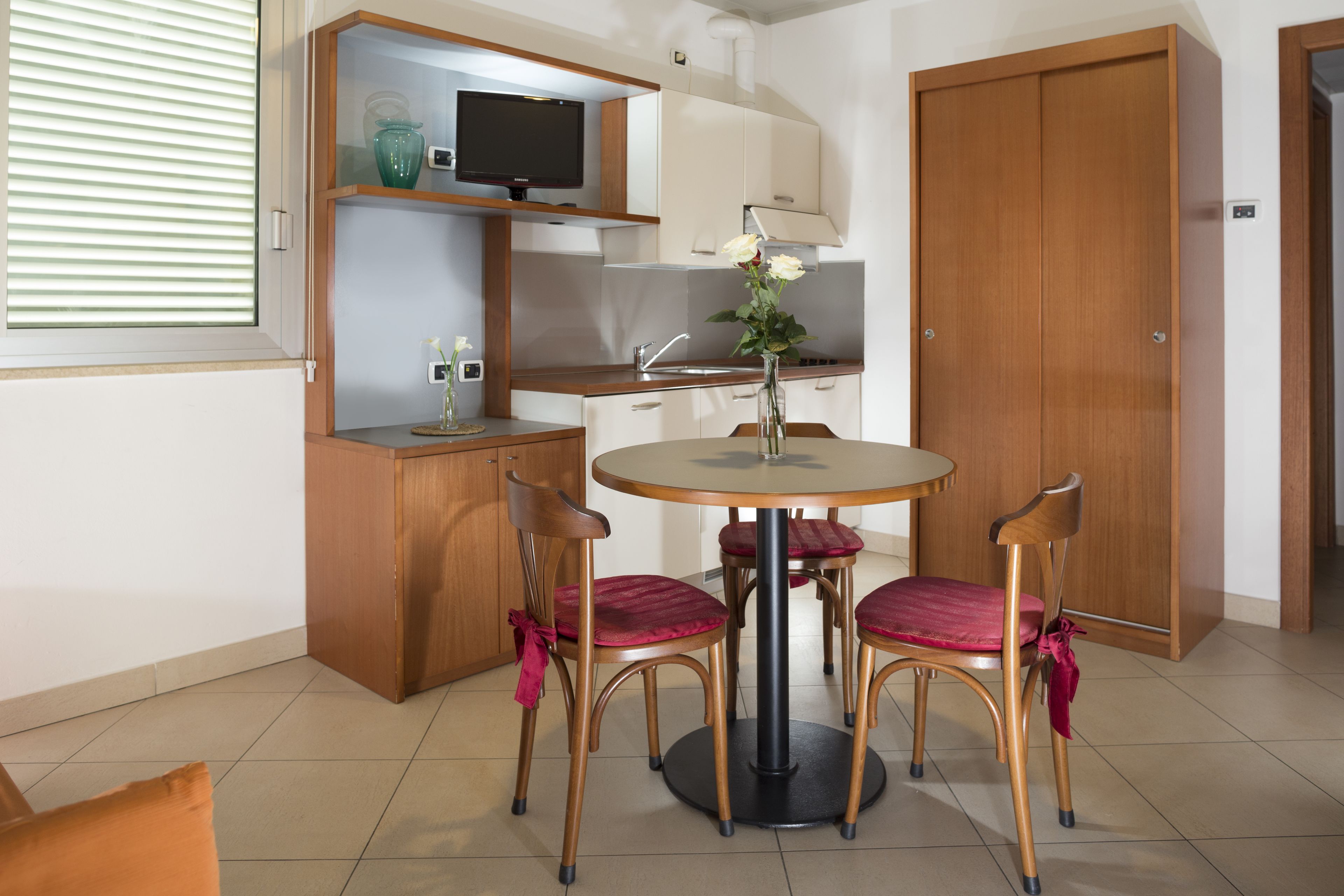 Uma cozinha compacta com uma mesa de jantar, cadeiras e uma TV em uma prateleira.