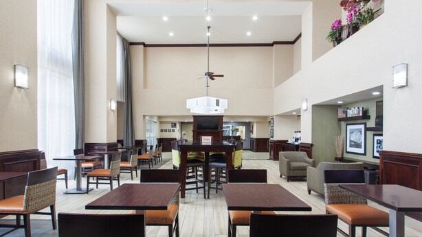 Um hall de hotel espaçoso com várias mesas e cadeiras para refeições, uma área de estar central e uma televisão.