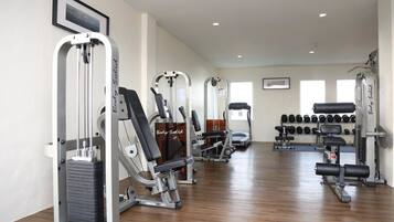 Uma academia com diversos equipamentos de exercício, halteres e um banco.
