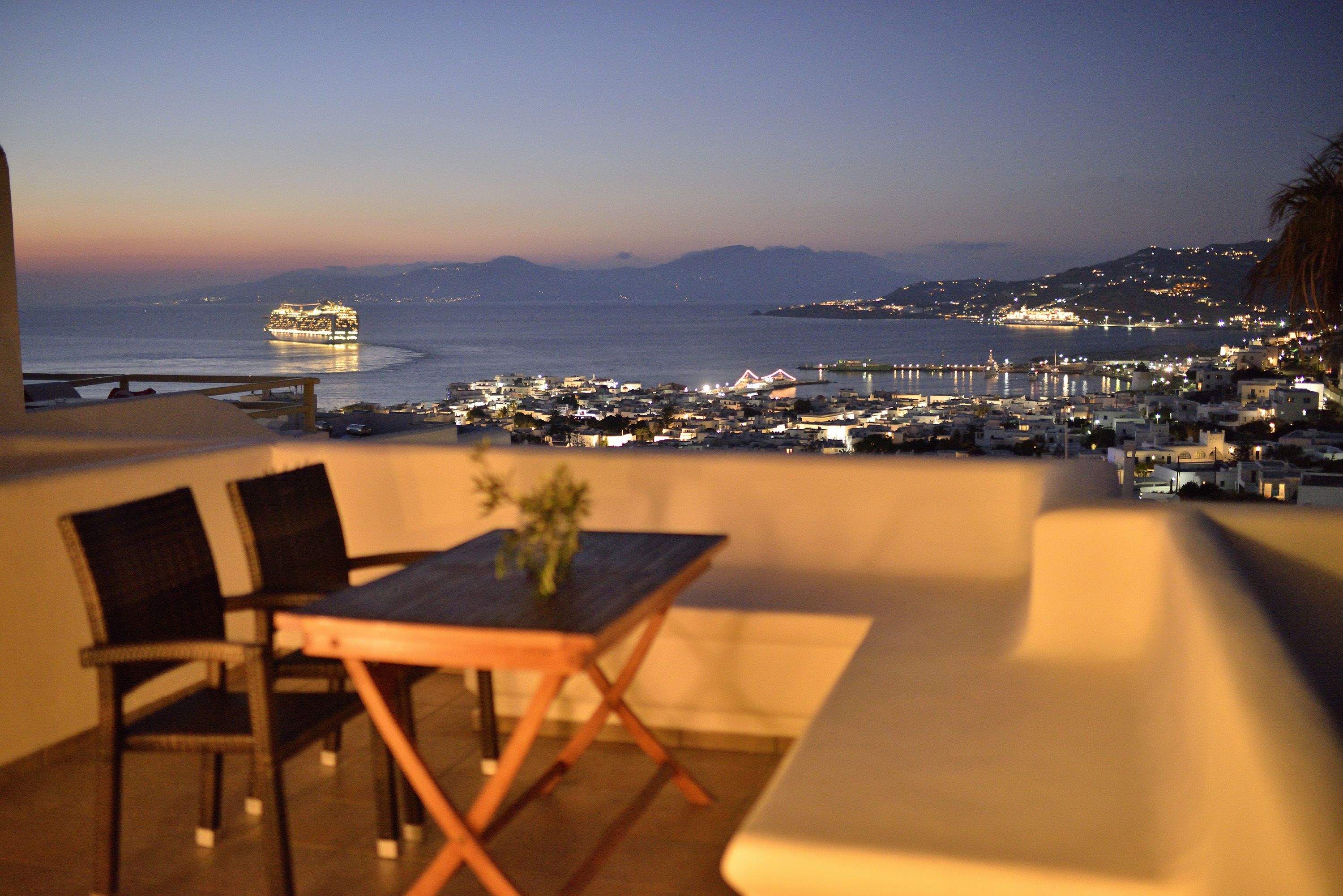 Um terraço com mesa e cadeiras, com vista para uma cidade costeira com edifícios e um corpo de água.