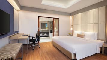 Quarto de hotel moderno com cama grande, escrivaninha, cadeira e televisão.