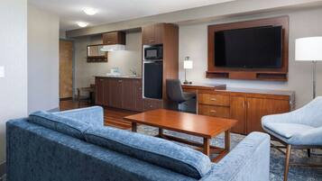 Quarto de hotel com cozinha compacta, televisão de tela plana na parede, sofá, mesa de jantar e luminária.