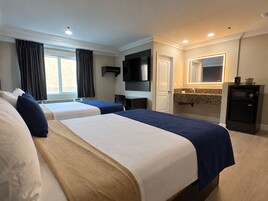 Quarto de hotel com duas camas, televisão de tela plana, escrivaninha pequena, espelho e minibar.