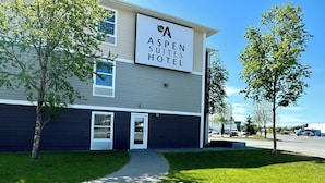 Edifício do Aspen Suites Hotel, com uma placa, entrada pavimentada e área gramada com árvores.