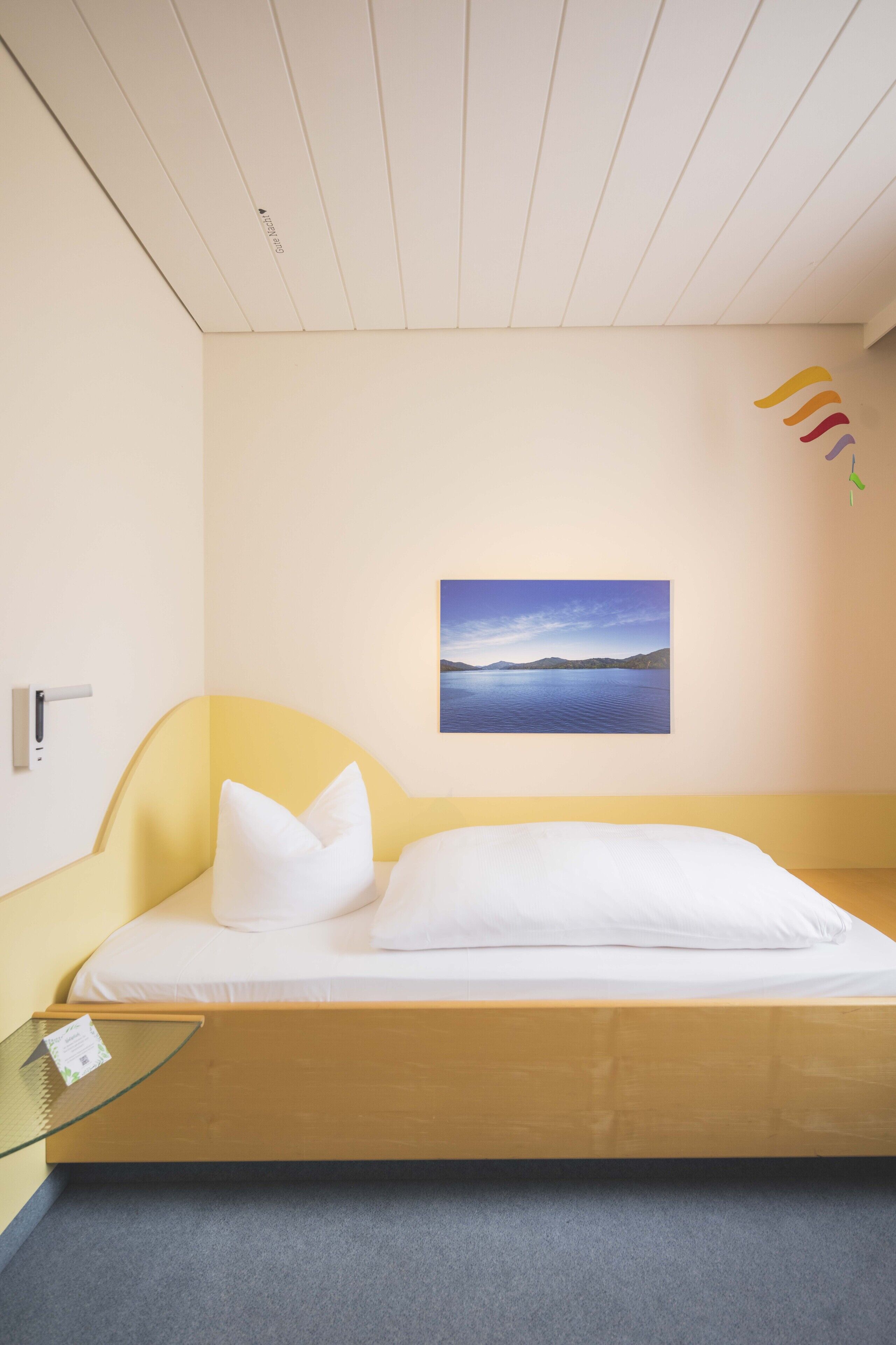 Quarto com cama, uma mesinha e um quadro na parede.