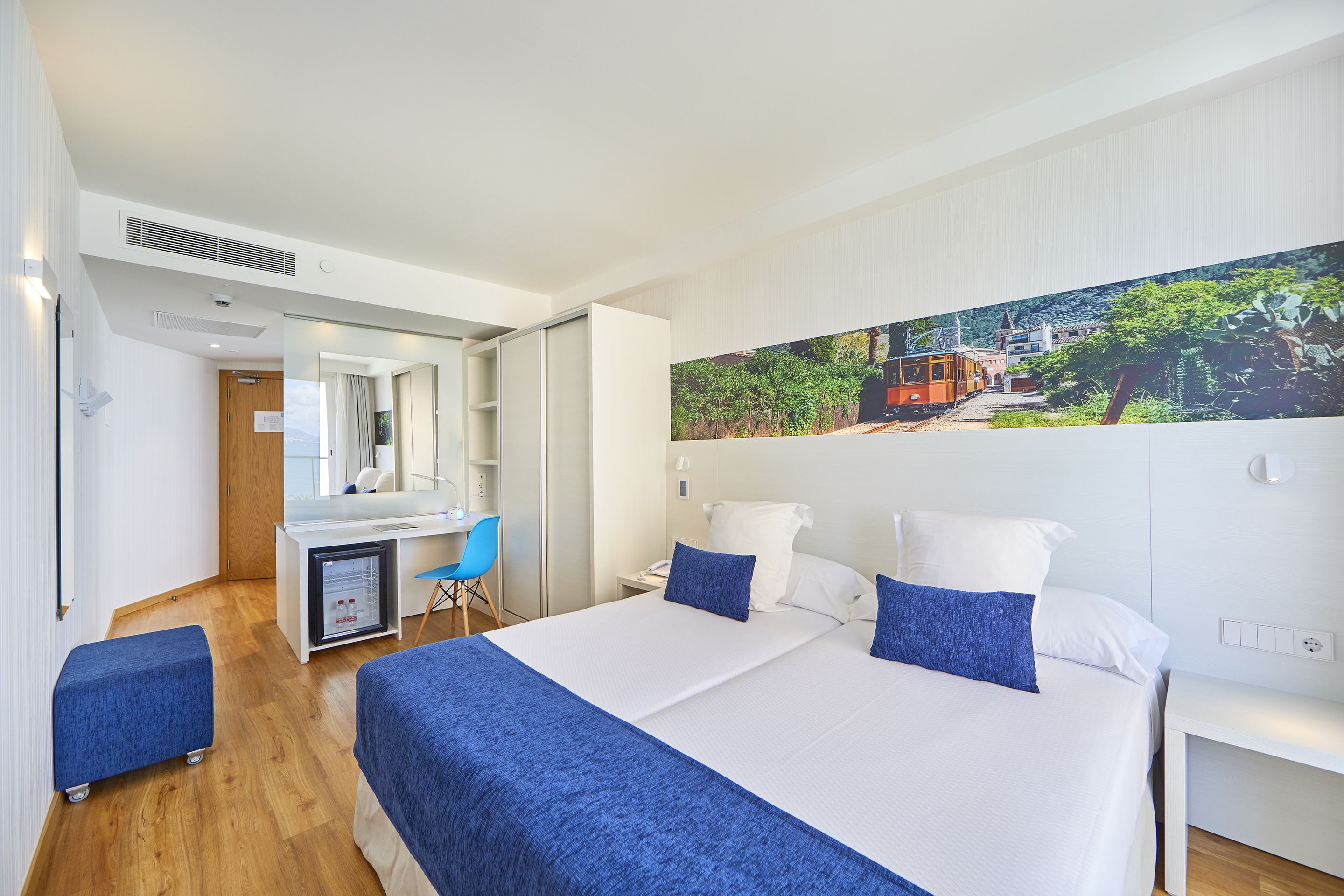 Quarto de hotel moderno com uma cama grande, uma escrivaninha, uma cadeira e uma pequena cozinha.