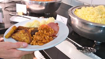 Buffet com diversos pratos, incluindo torradas, feijão, bacon e ovos mexidos.