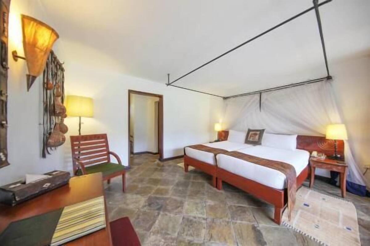 Quarto com cama, duas mesas de cabeceira, uma cadeira, escrivaninha e abajur.