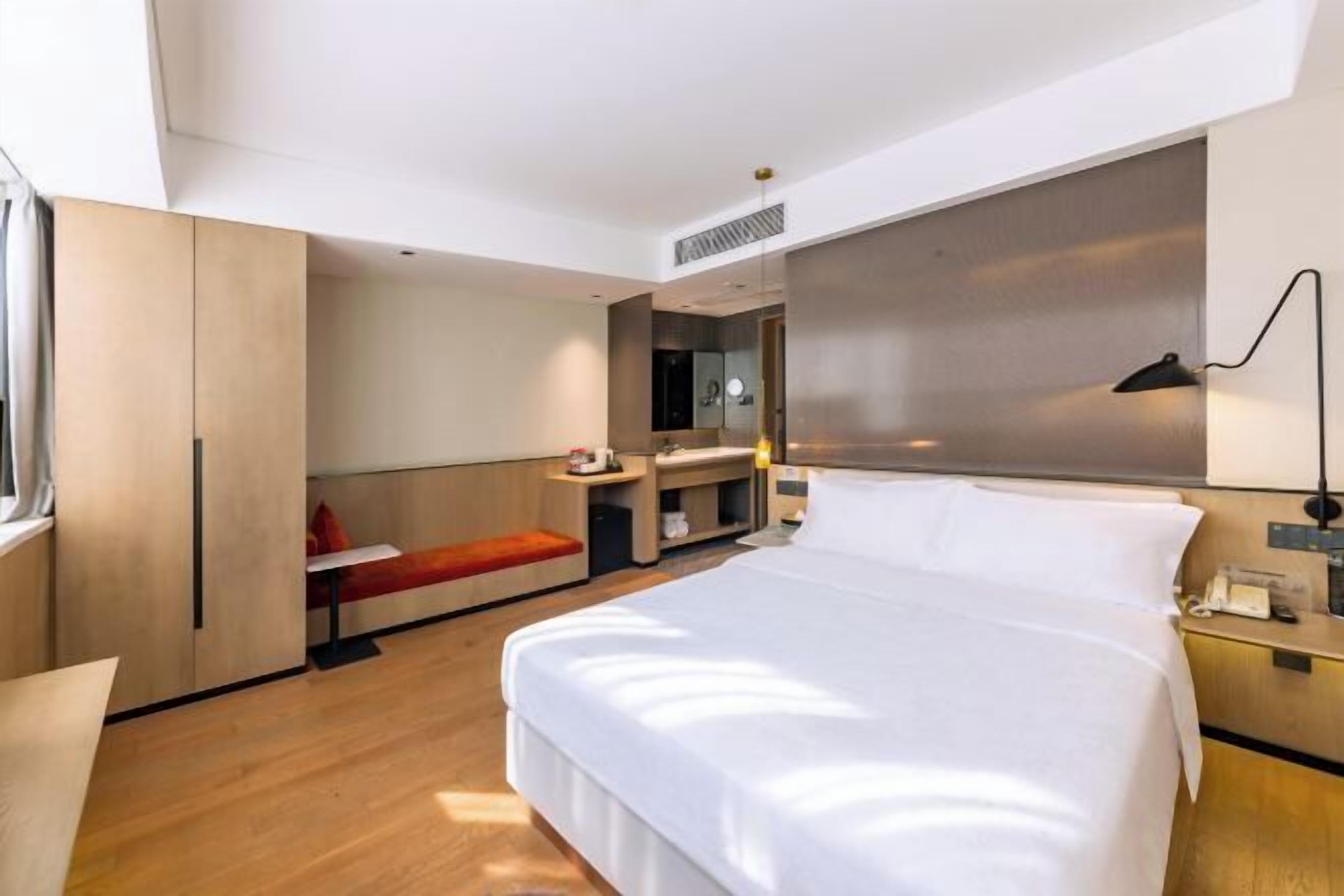 Quarto de hotel moderno com uma cama grande, uma escrivaninha, uma cadeira e um guarda-roupa.