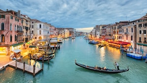 Um canal com gôndolas e barcos, cercado por edifícios históricos com varandas e lojas.