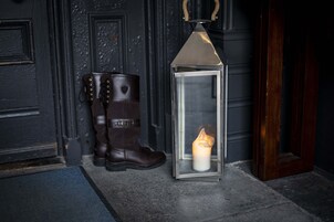 Um par de botas de couro marrom ao lado de uma vela acesa num candeeiro de vidro sobre um chão de pedra.