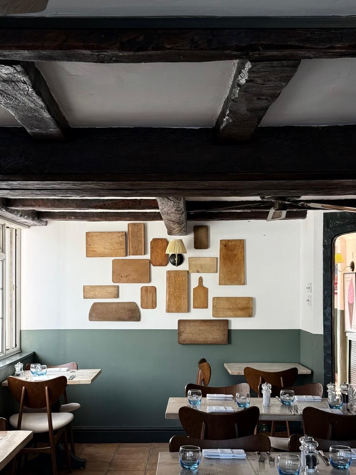 Interior de restaurante com vigas de madeira aparente, diversos painéis de madeira na parede e mesas preparadas para refeições.