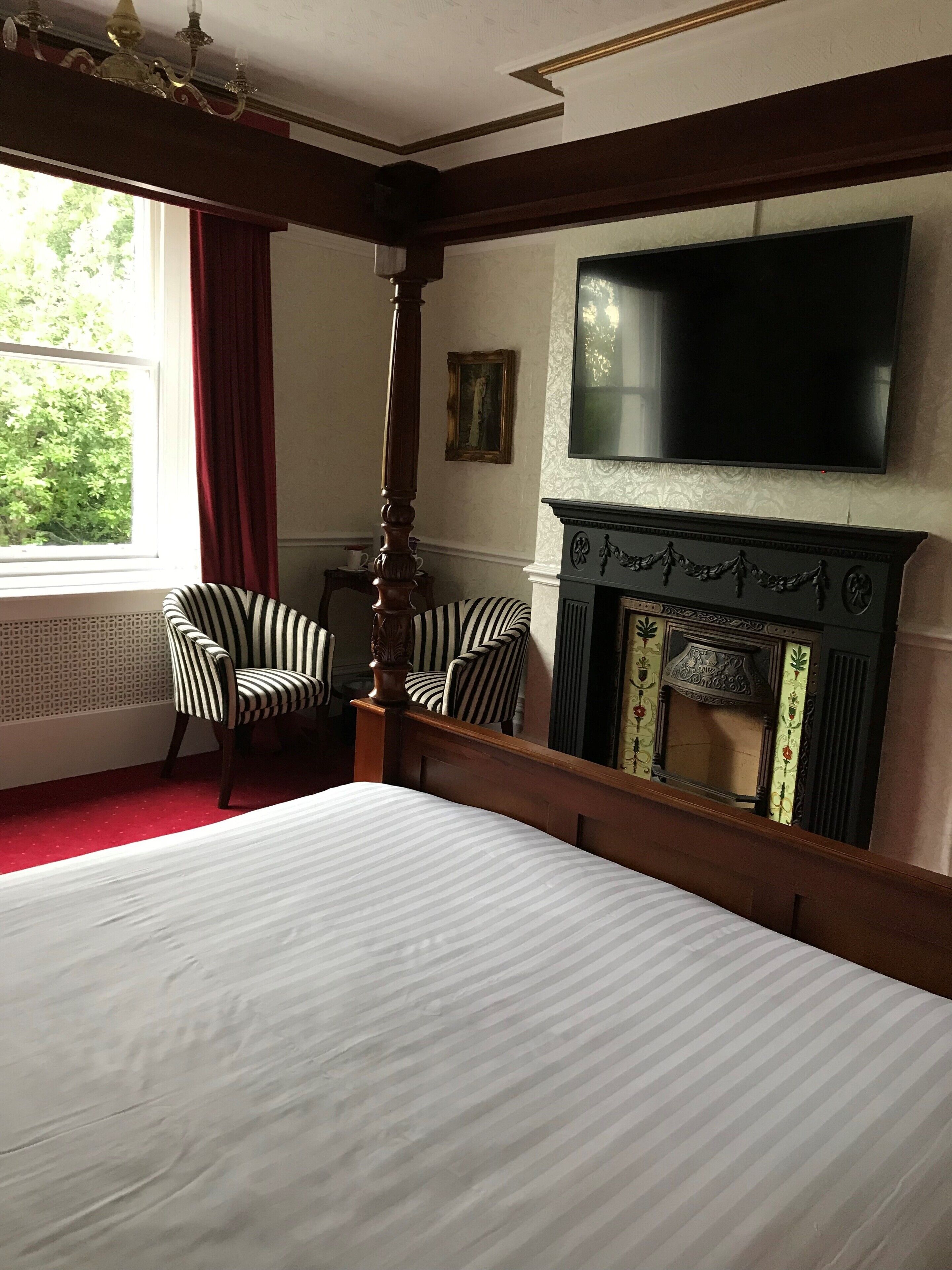 Quarto de hotel com uma cama grande, lareira, televisão na parede e duas cadeiras listradas.
