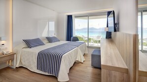 Quarto de hotel com uma cama grande, telefone ao lado da cama, escrivaninha e vista para o mar.