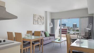Quarto de hotel moderno com área de jantar, sofá e varanda com vista para a cidade.