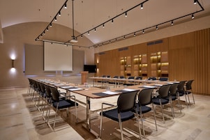 Uma sala de conferências com uma mesa comprida, cadeiras, uma tela de projetor e um pódio.