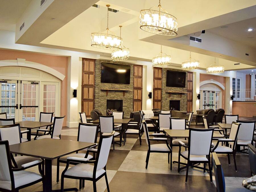 Uma sala de jantar ampla com várias mesas e cadeiras, uma lareira de pedra e lustres modernos.