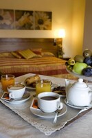 Uma bandeja de café da manhã com café, suco, doces e uma cesta de frutas sobre uma mesa em um quarto de hotel.