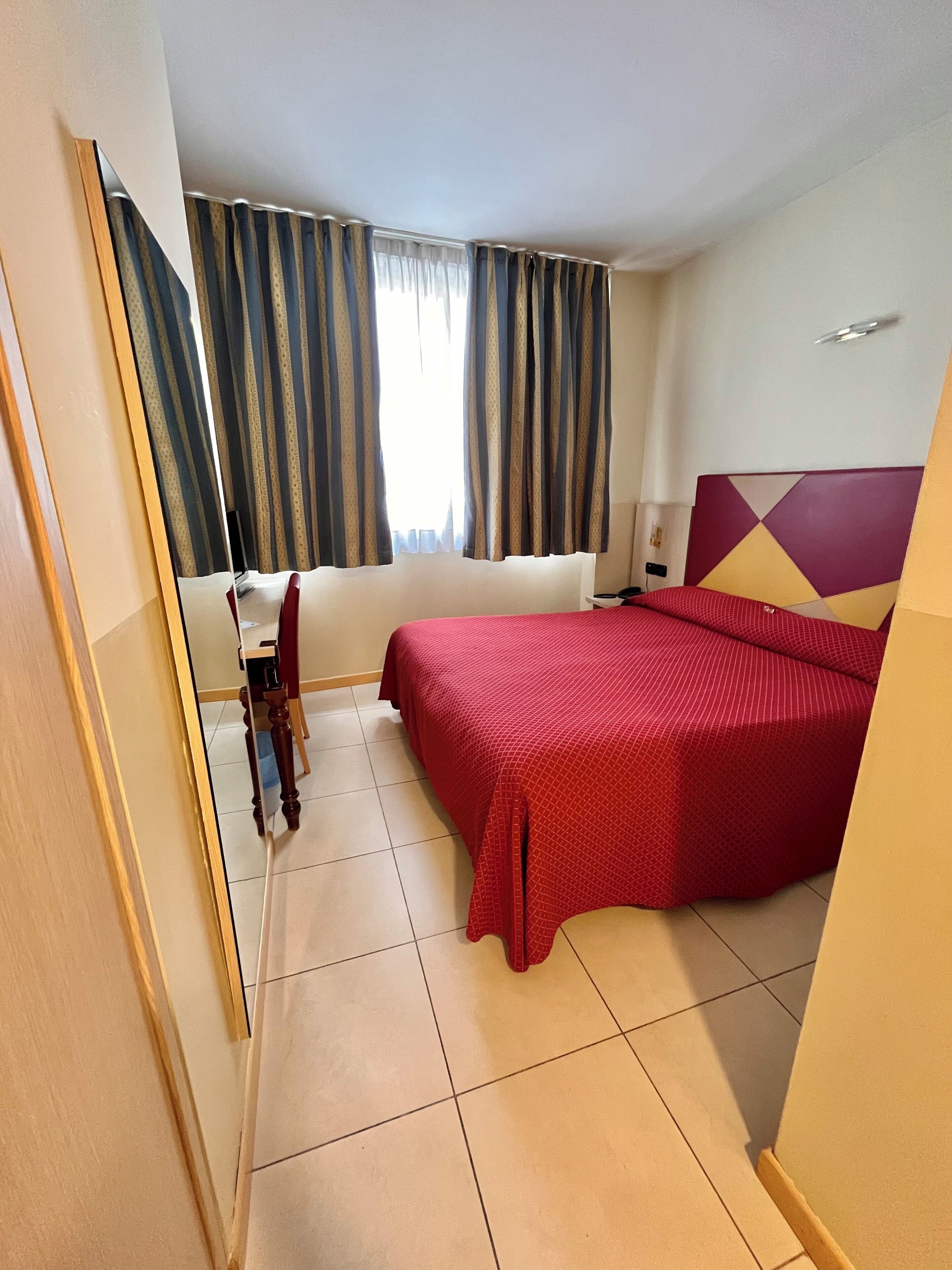 Quarto de hotel com cama, escrivaninha e janela com cortinas.