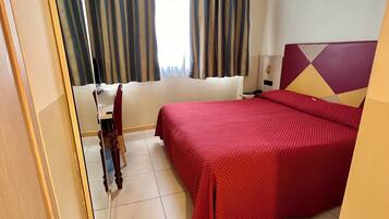 Quarto de hotel com cama, escrivaninha e janela com cortinas.