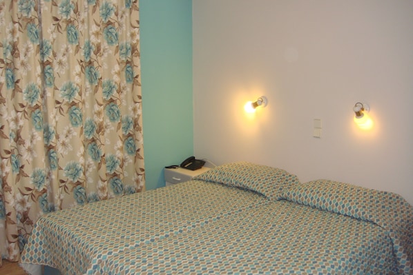 Quarto com cama, mesa de cabeceira, telefone e duas luzes fixadas na parede.