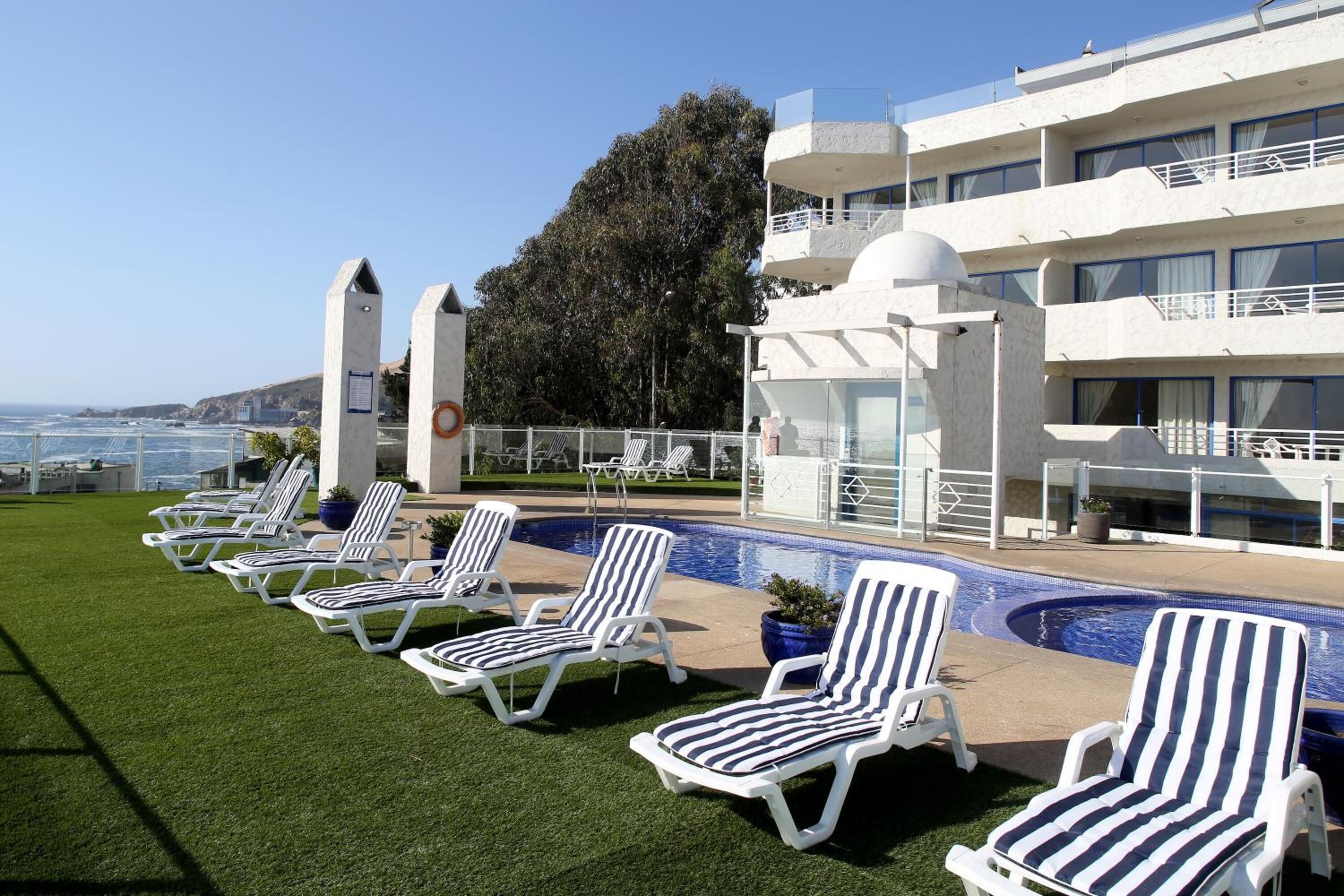 Área da piscina com espreguiçadeiras e vista para o mar.