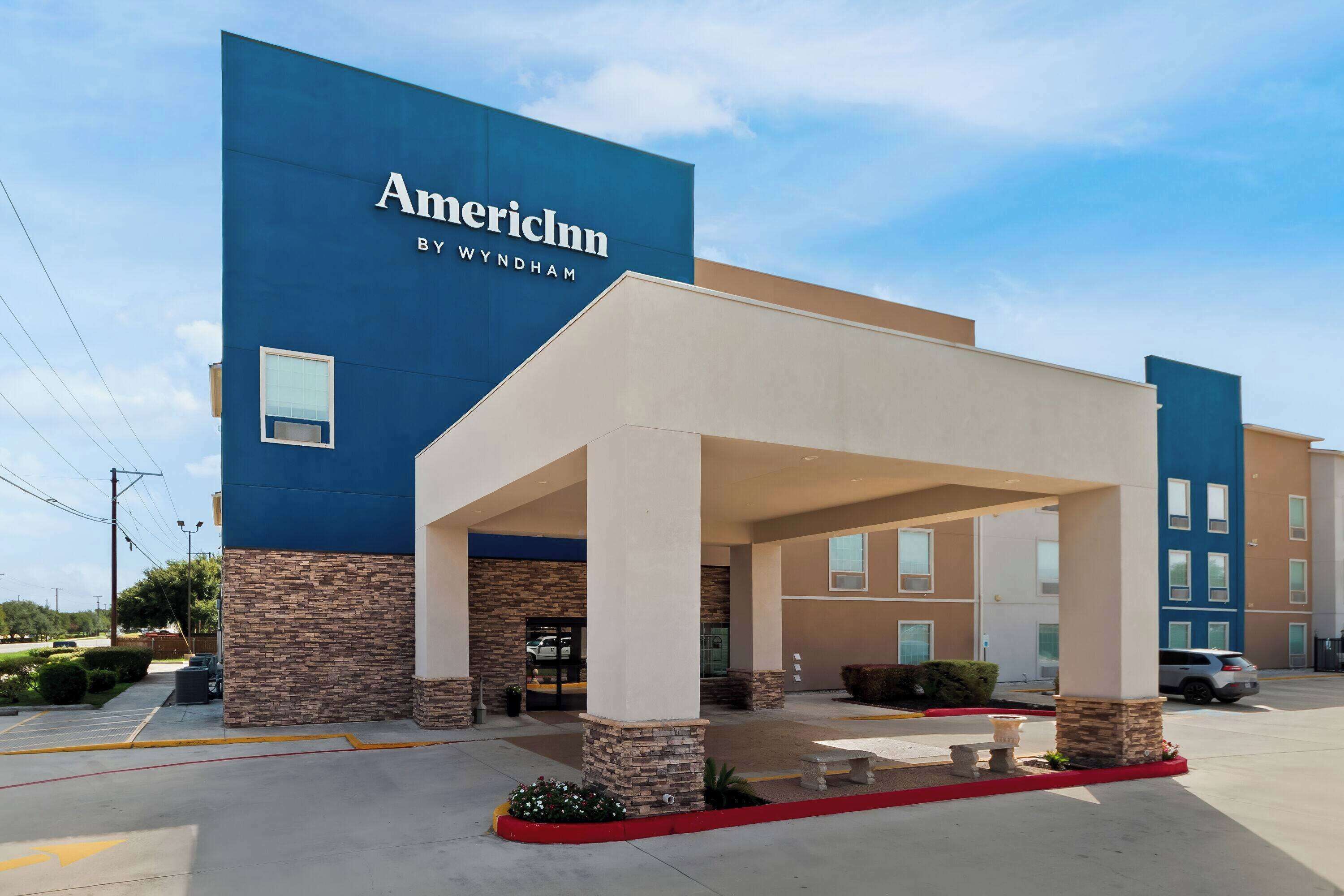 Um hotel AmericInn by Wyndham com entrada coberta, área de estar externa e estacionamento.