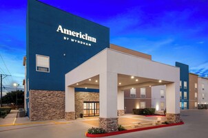 Edifício do American Inn by Wyndham com entrada coberta, fachada de pedra e céu claro.