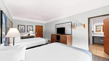 Quarto de hotel com duas camas, uma televisão, uma mesa com abajur e banheiro visível por uma porta aberta.