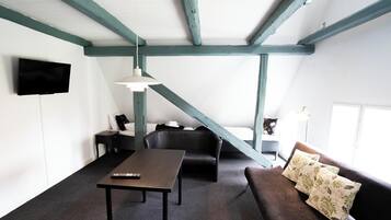Quarto moderno e bem iluminado com sofá, mesa e televisão na parede.