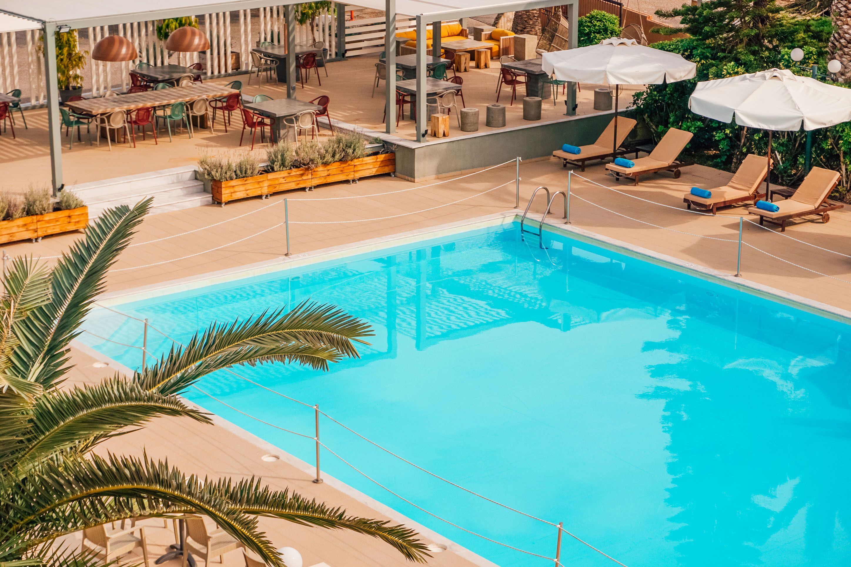 Área da piscina com espreguiçadeiras, guarda-sóis e mobiliário para área externa.