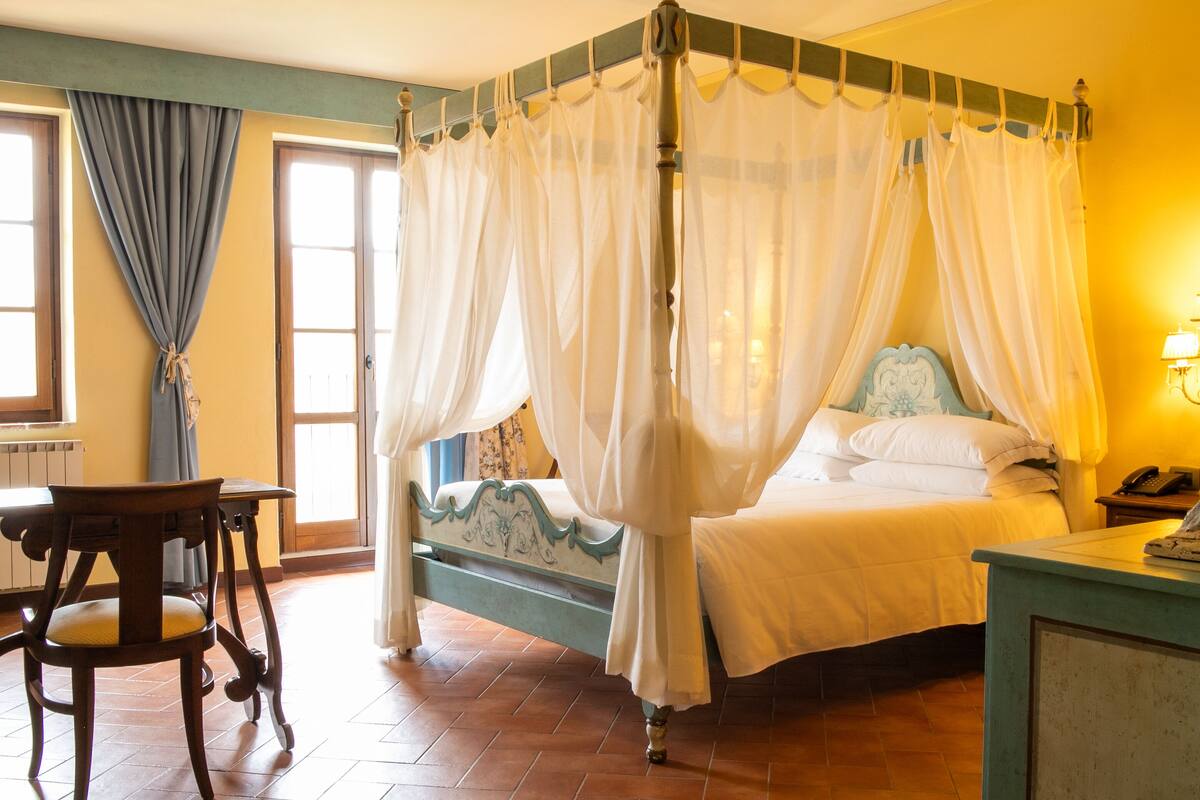 Quarto com cama de dossel, uma cadeira de madeira e mesa de cabeceira.