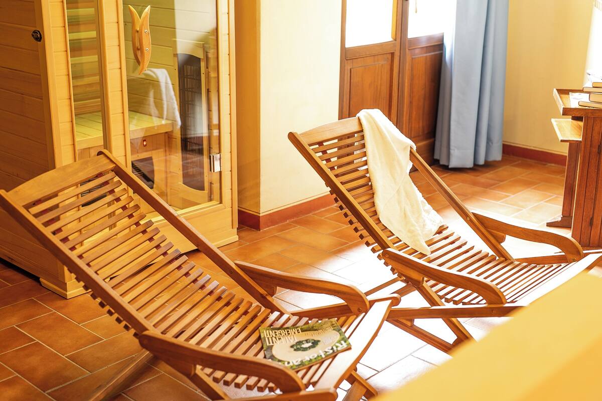 Duas poltronas de madeira com toalhas, uma mesa de madeira e uma porta de vidro que dá para um quarto.