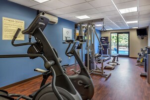 Centro de ginástica com equipamentos de exercício, esteira e televisão na parede.