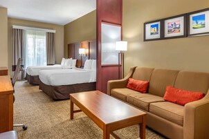 Quarto de hotel com duas camas, um sofá, uma escrivaninha e um abajur.