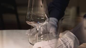 Um close-up de uma taça de vinho sobre uma mesa, com a mão enluvada de alguém segurando-a.