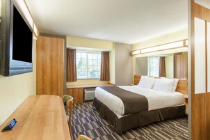 Quarto de hotel com uma cama, escrivaninha, cadeira, televisão e janela com cortinas.