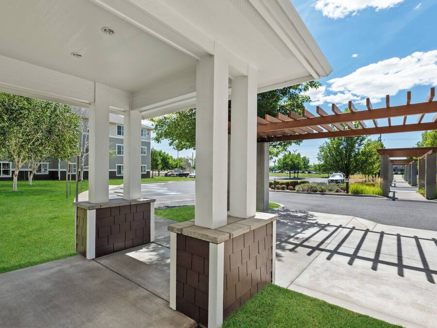 Um espaço ao ar livre coberto com pérgola, um vaso de tijolos e um caminho que leva à entrada de um edifício.