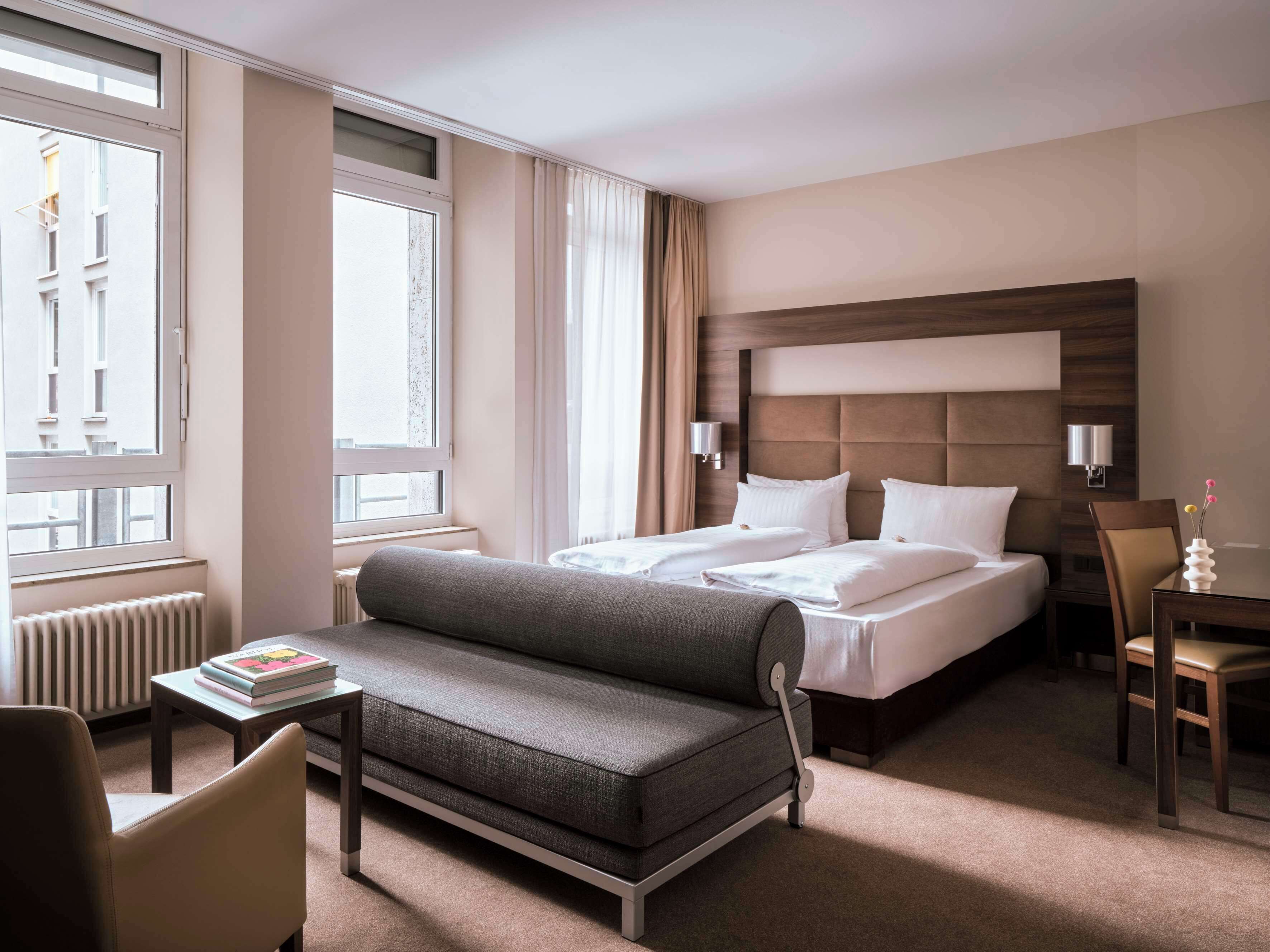 Quarto de hotel com uma cama grande, um sofá, uma mesa pequena e uma cadeira.