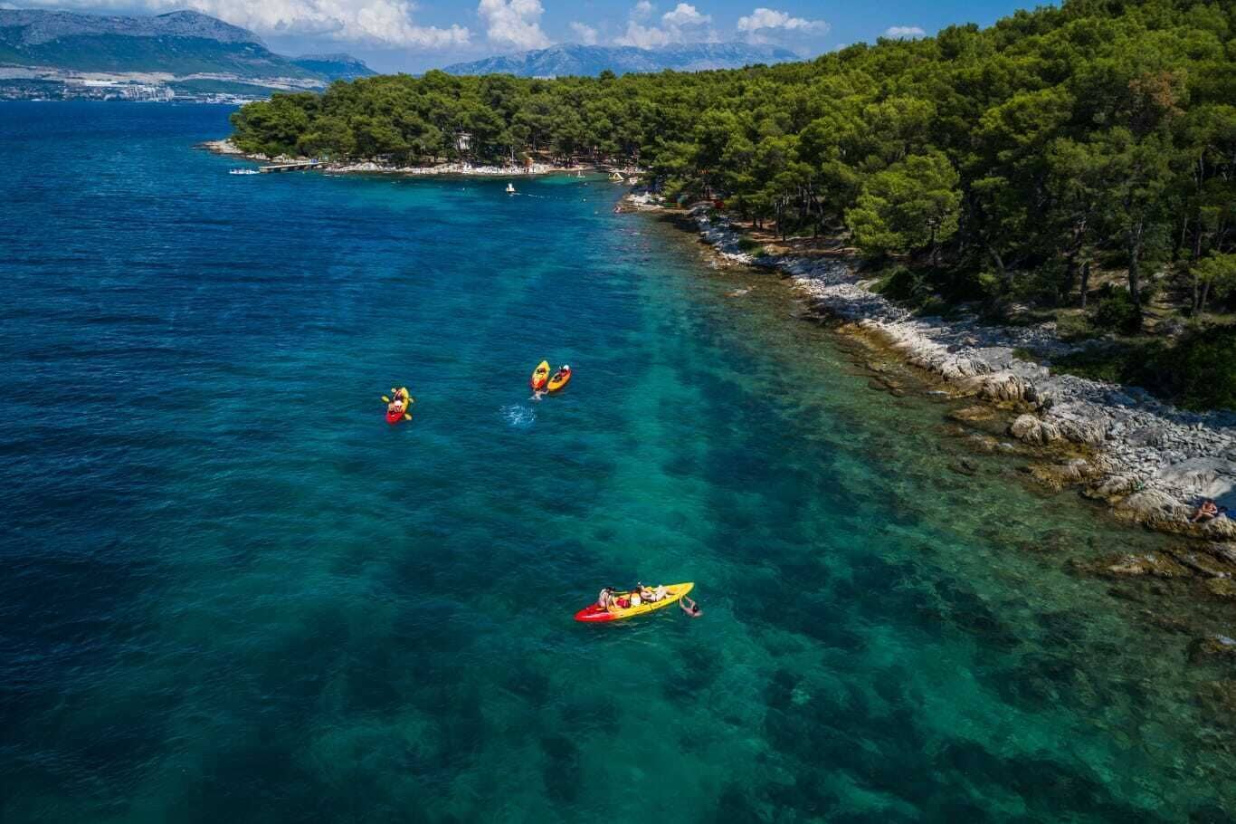 Uma área costeira com águas azul-turquesa translúcidas, margens rochosas e árvores verdes densas.