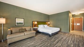 Quarto de hotel com cama, sofá, mesa de cabeceira e luminária fixada na parede.