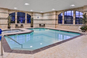 Uma grande piscina interior com um deck ladrilhado, área de estar e amplas janelas.