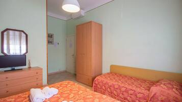 Quarto com duas camas, um guarda-roupa de madeira, uma televisão em uma cômoda e uma luminária no teto.