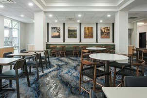 Uma sala de jantar com várias mesas e cadeiras, um tapete estampado e obras de arte nas paredes.