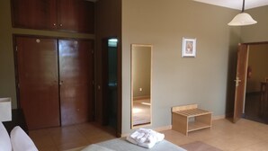 Quarto de hotel com cama, guarda-roupa de madeira, um pequeno banco e um espelho.