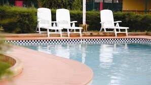 Piscina com borda xadrez, rodeada por espreguiçadeiras brancas.