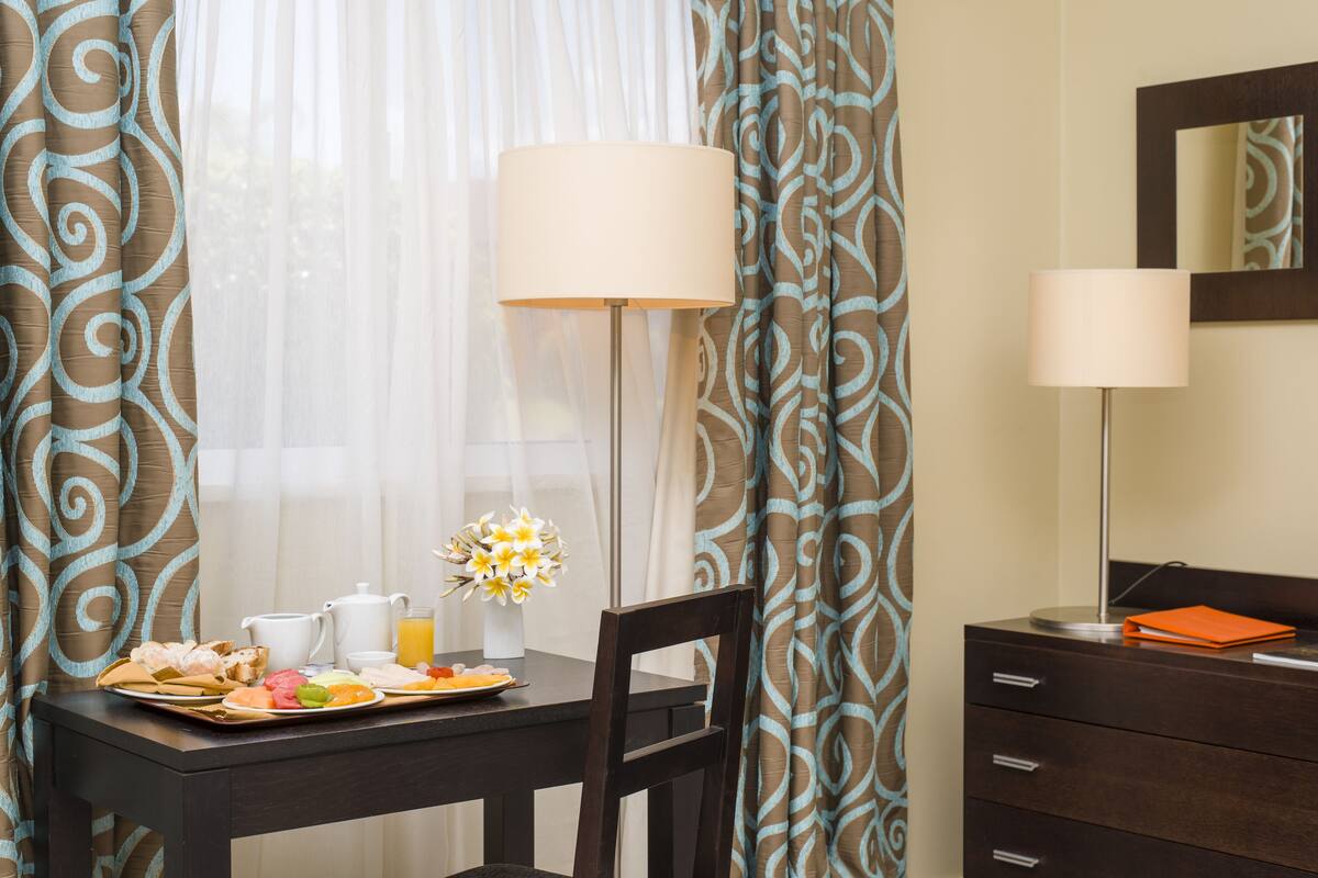 Quarto de hotel com uma mesa de jantar posta para o café da manhã, uma luminária e um espelho.