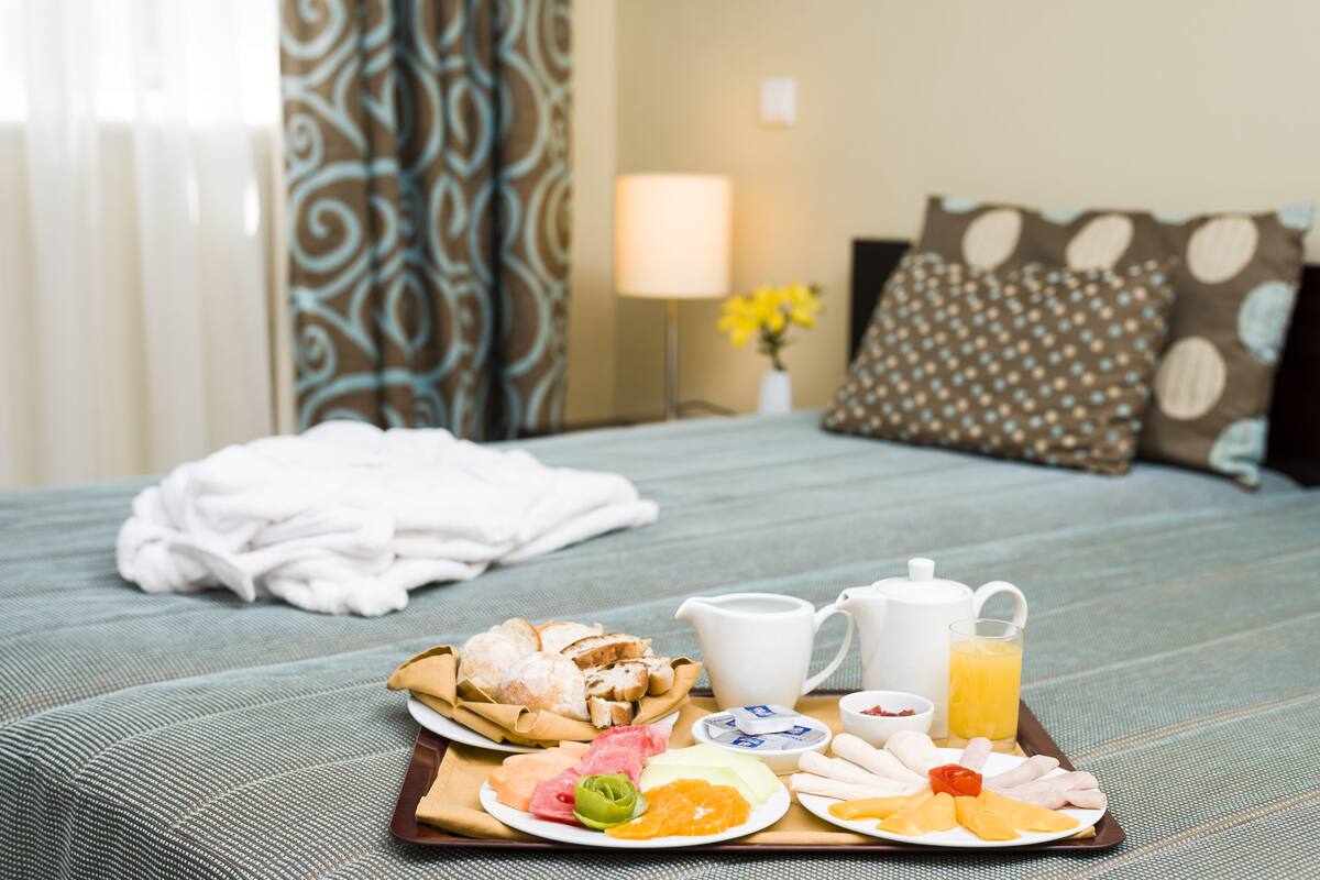 Uma bandeja de café da manhã bem arrumada, com diversos alimentos e bebidas, sobre a cama em um quarto de hotel.
