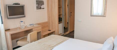 Quarto de hotel com cama, escrivaninha e cadeira, televisão, guarda-roupa e um quadro na parede.