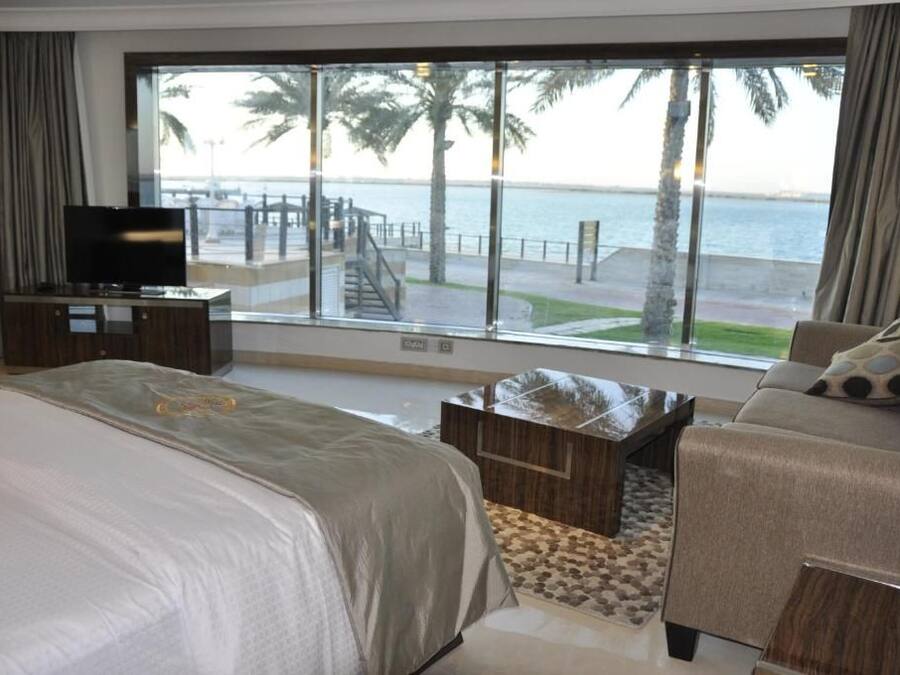 Quarto de hotel com uma janela ampla que oferece vista para uma praia e palmeiras.